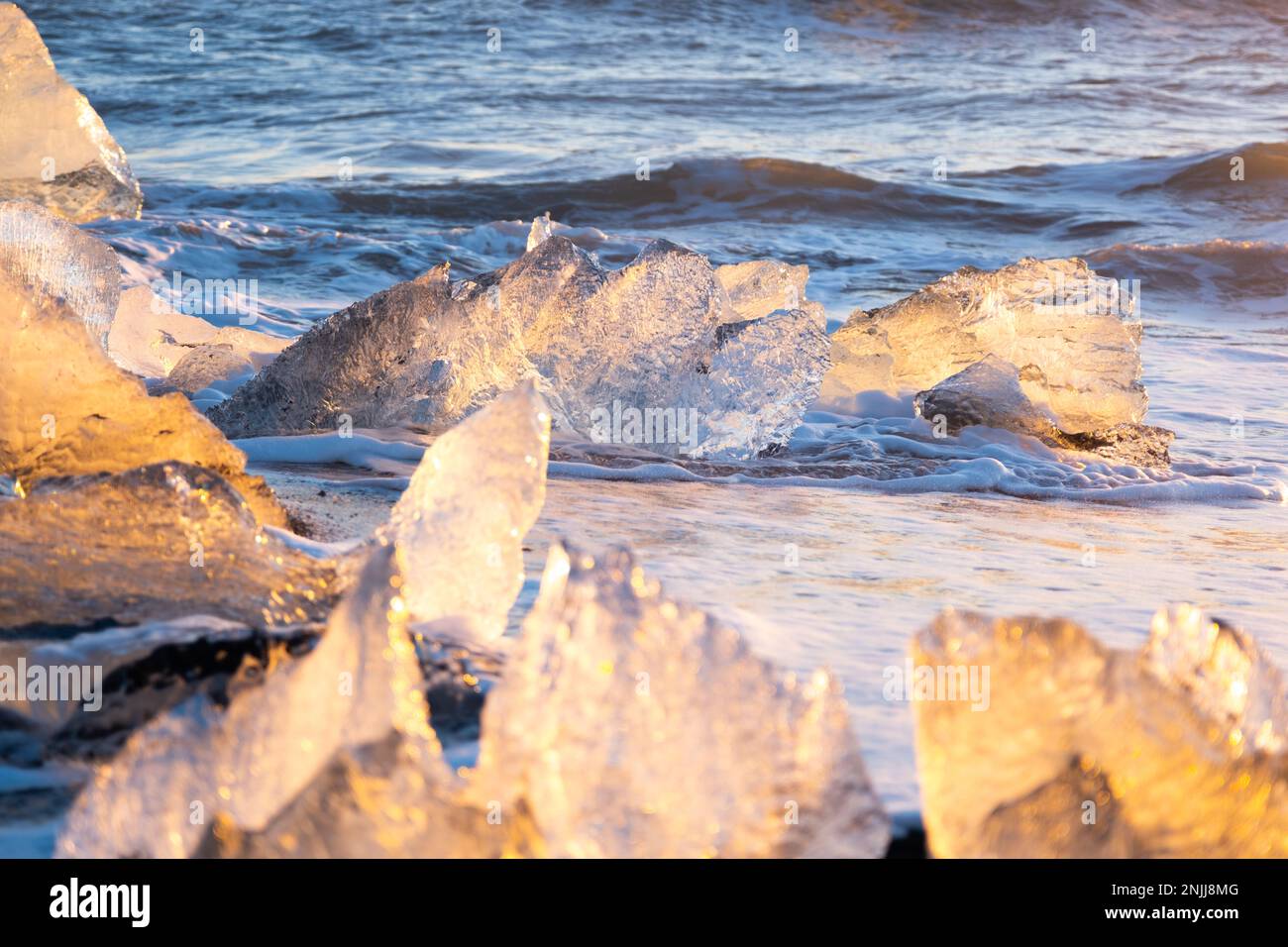 Pure glacier ice shining at sunset. Black volcanic sand at ocean coast ...