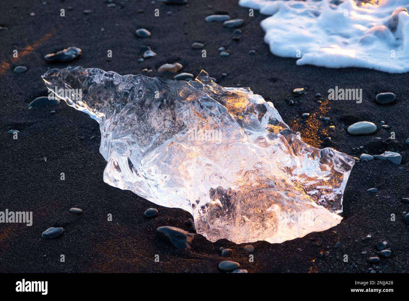 Pure glacier ice shining at sunset. Black volcanic sand at ocean coast ...