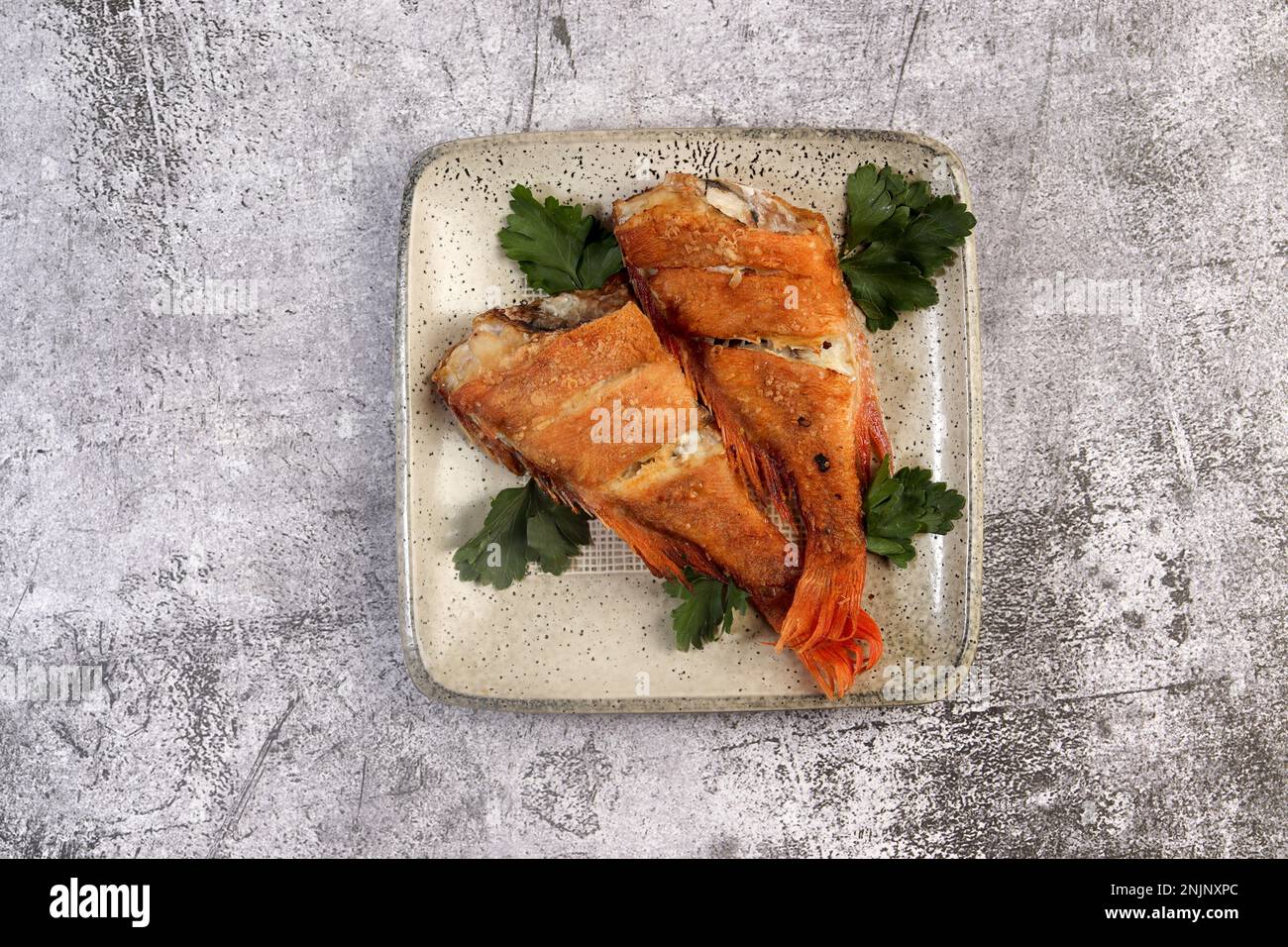 Pan Fried Rose fish with herbs on a square plate on a dark background ...