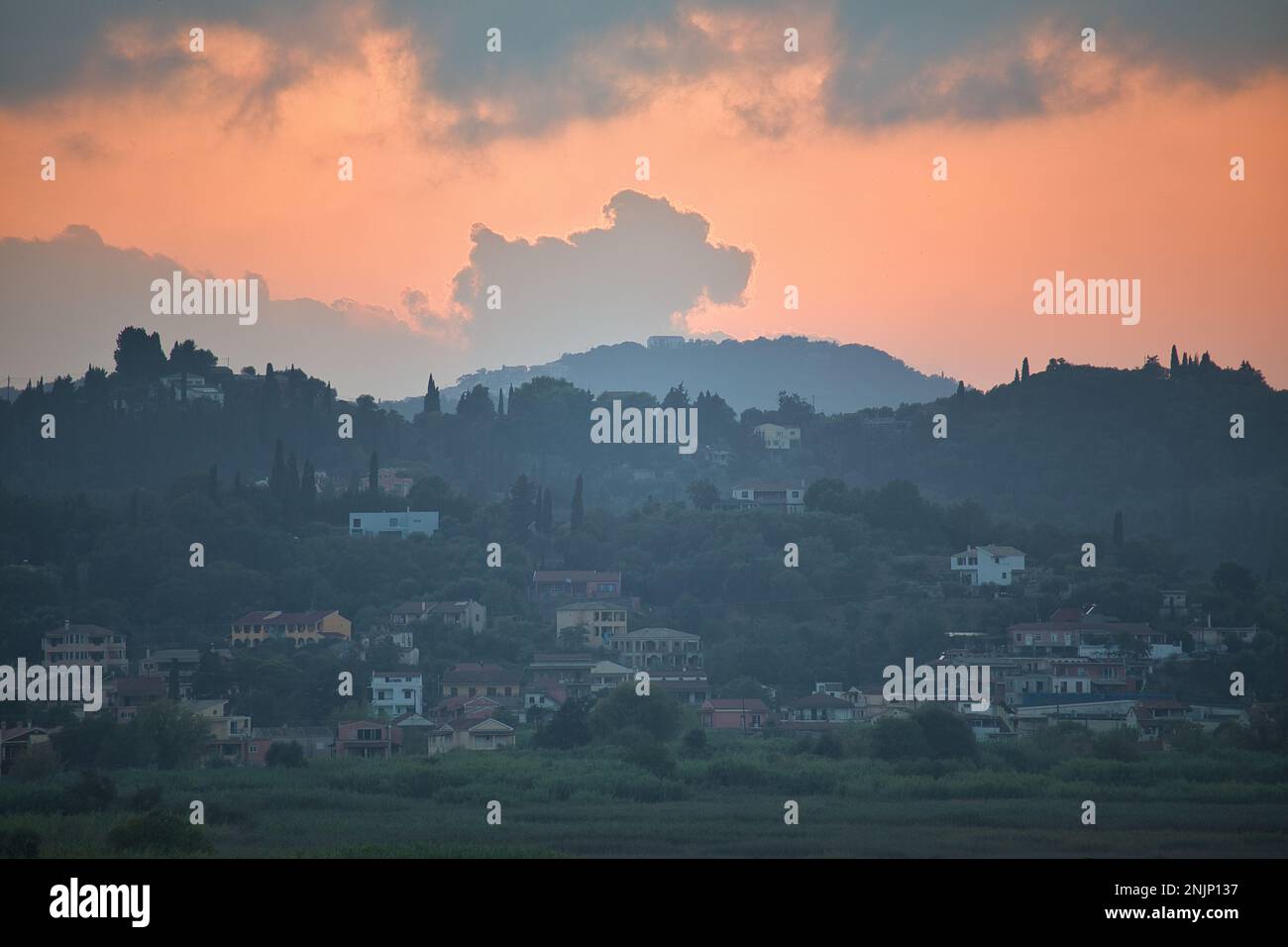 Sunset on a hillside landscape of houses and trees, the sky shines in ...