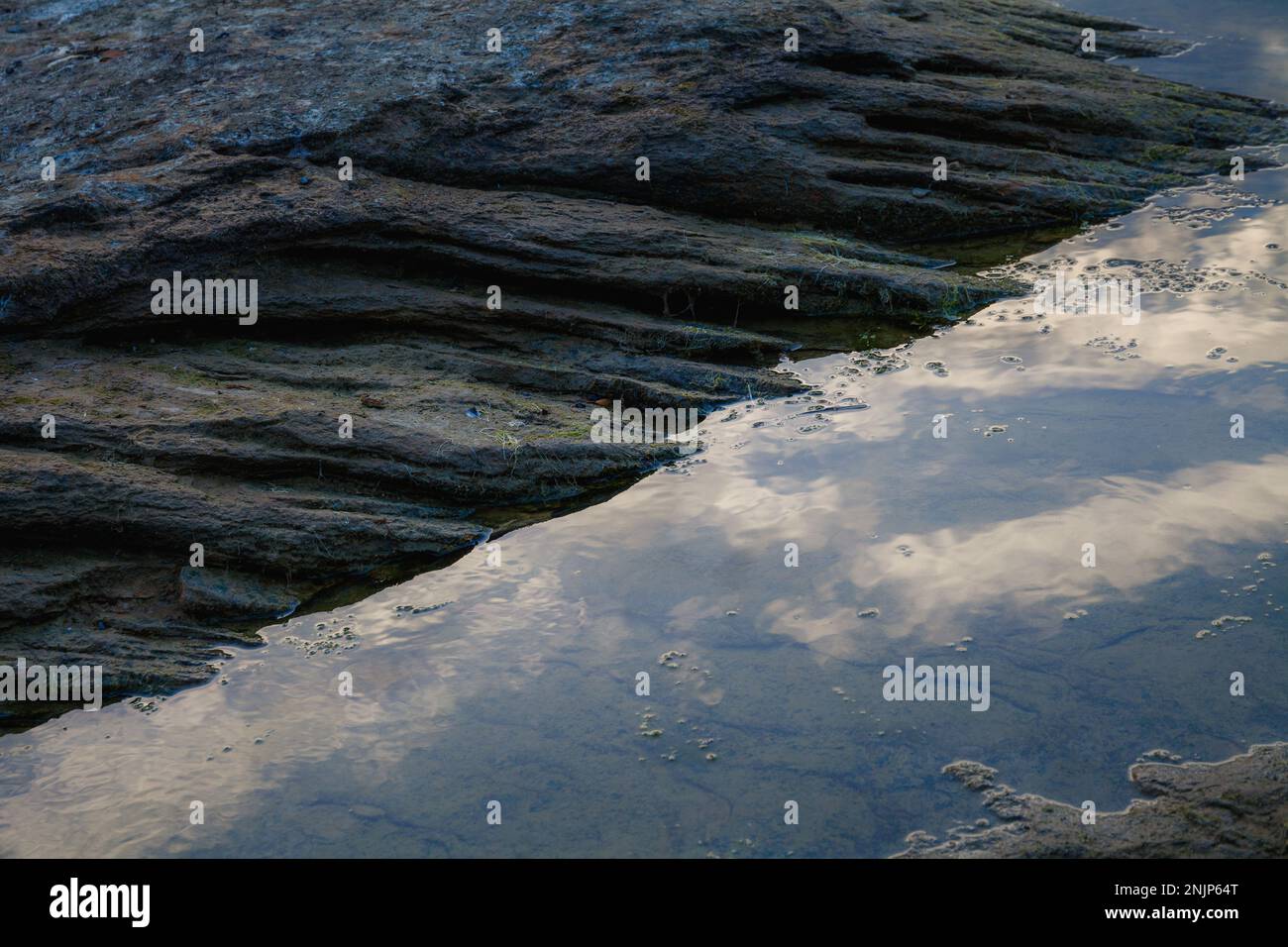 Detail of a immersed into sea water at sunset. Rock full of layers and ...