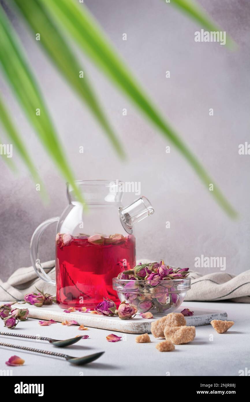 Beautiful flower pink sweet tea in glass teapot with dry rose buds and ...