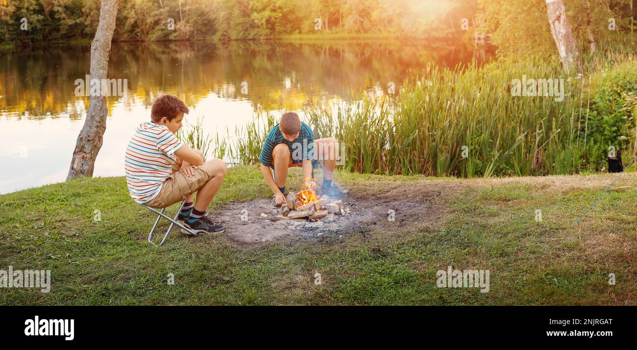 Two teenagers lighting a campfire in nature near the lake Stock Photo ...