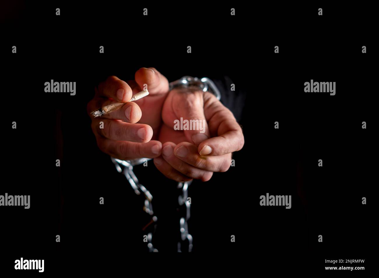 man's hands chained, with a cigarette in his fingers black background ...