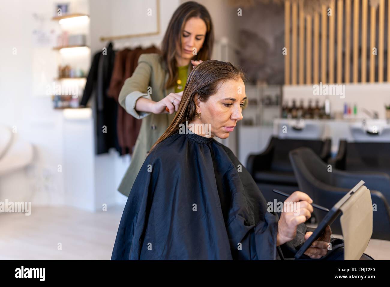 Professional hairstylist brushing hair of client sitting on chair in ...