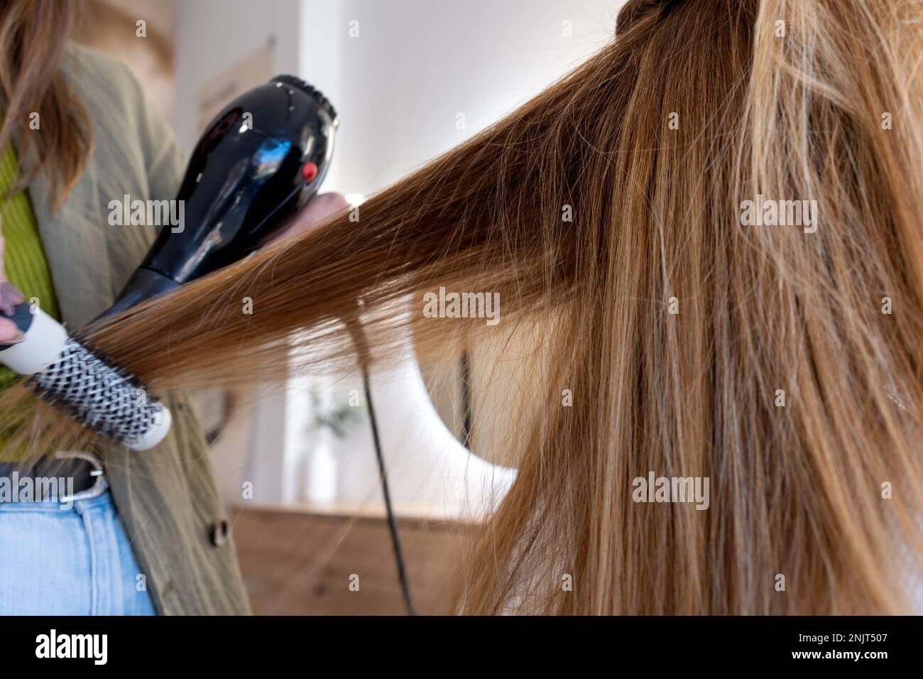 Crop unrecognizable female hairstylist using round comb and dryer to ...