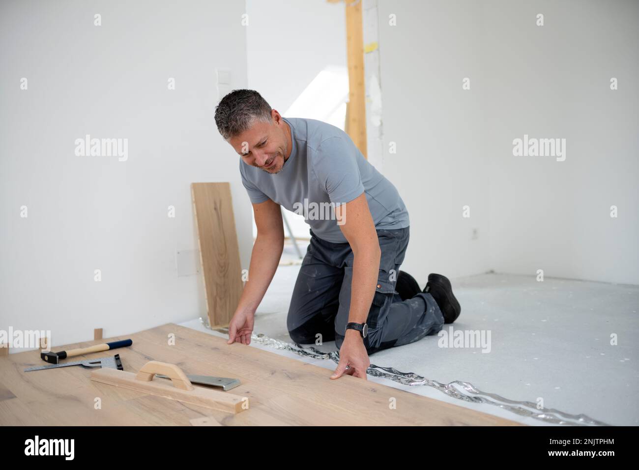 Middle aged man with grey hair and grey shirt laying parquet floor in ...