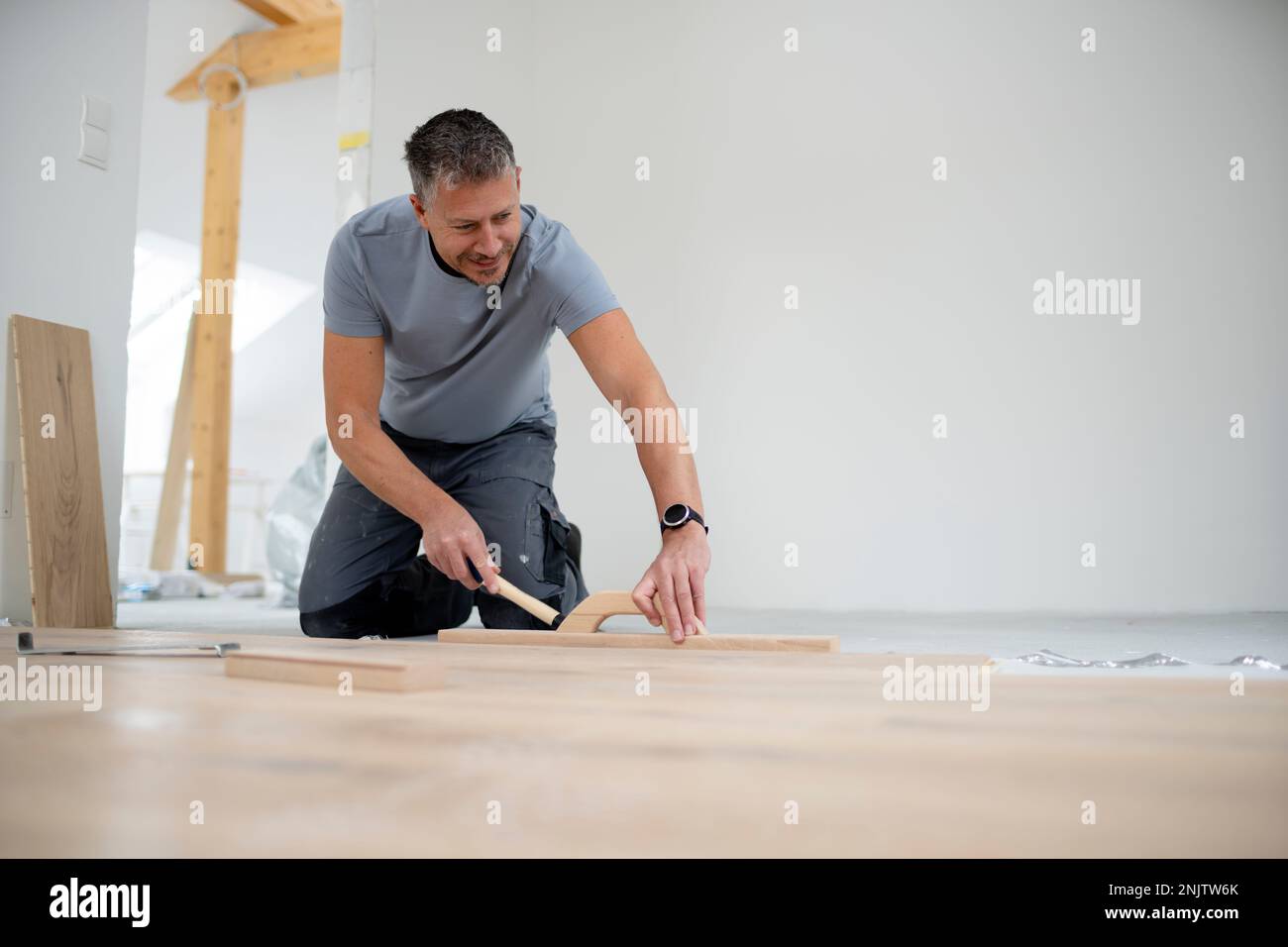 Middle aged man with grey hair and grey shirt laying parquet floor in ...