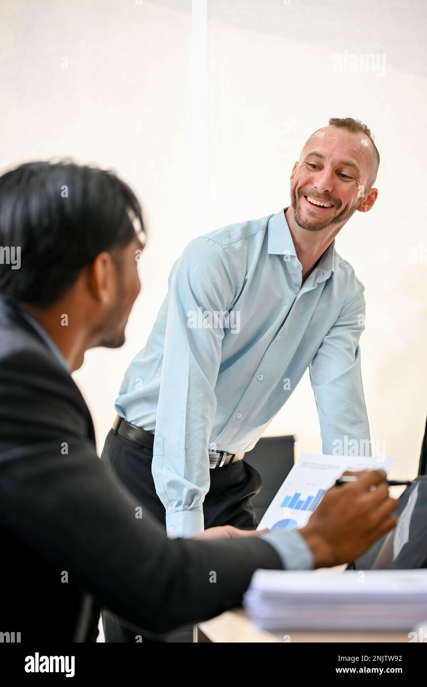 Happy caucasian male boss enjoys talking with his Asian male coworker ...