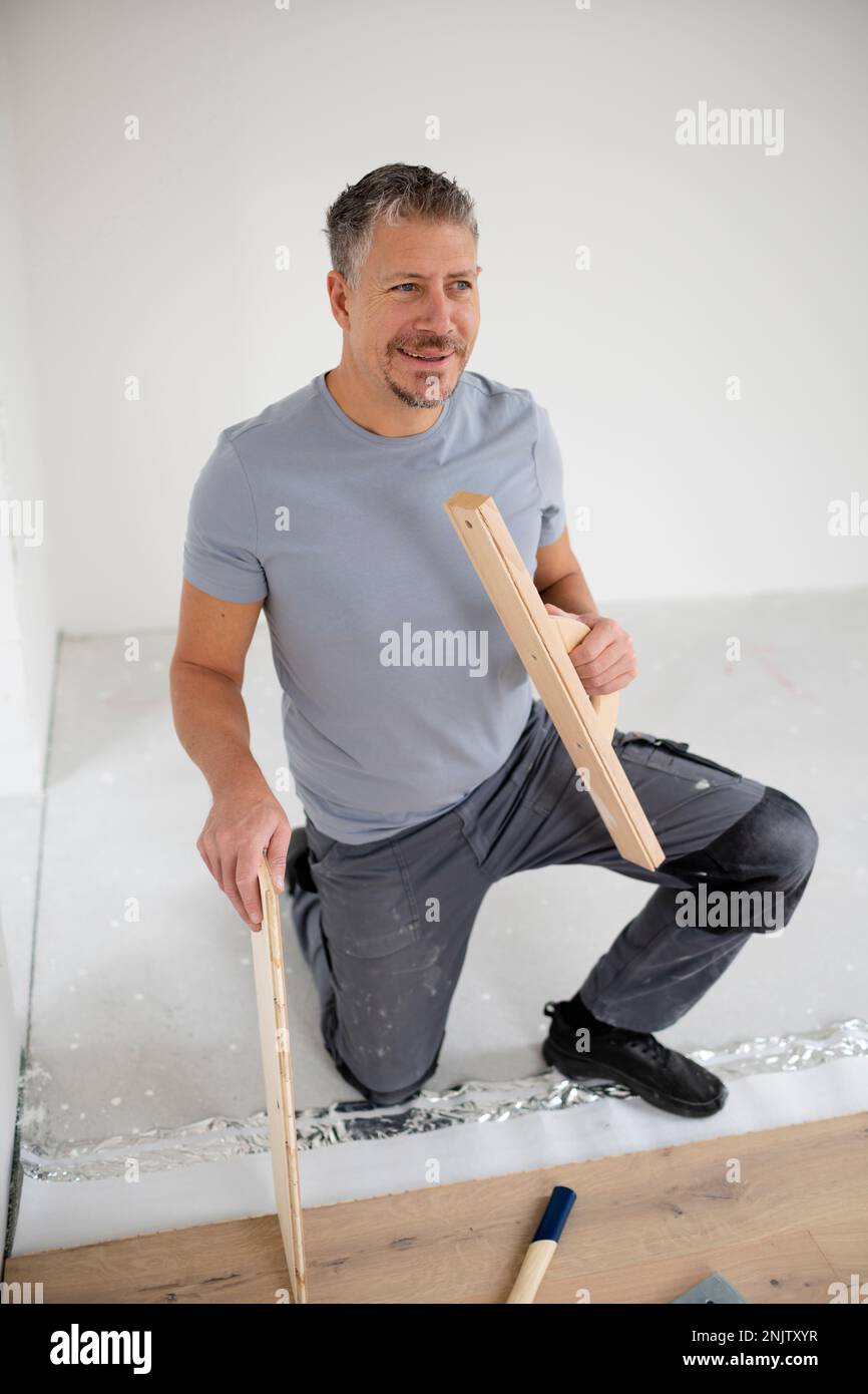 Middle aged man with grey hair and grey shirt laying parquet floor in ...