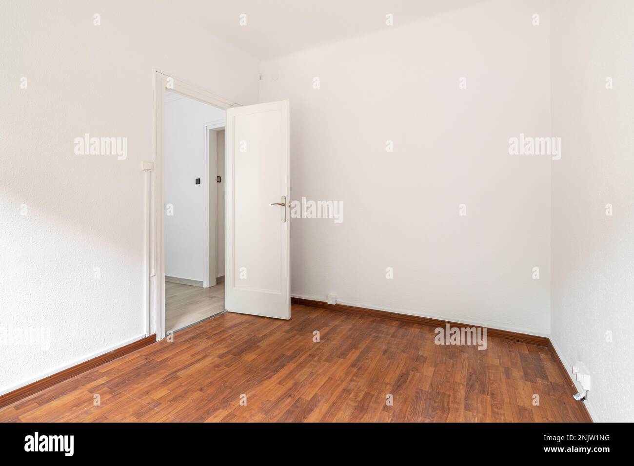 Empty spacious room well lit by daylight. The floor is dark brown wood ...