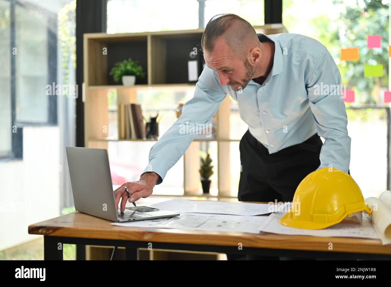 Smart engineer man in shirt using laptop and working with blueprints ...