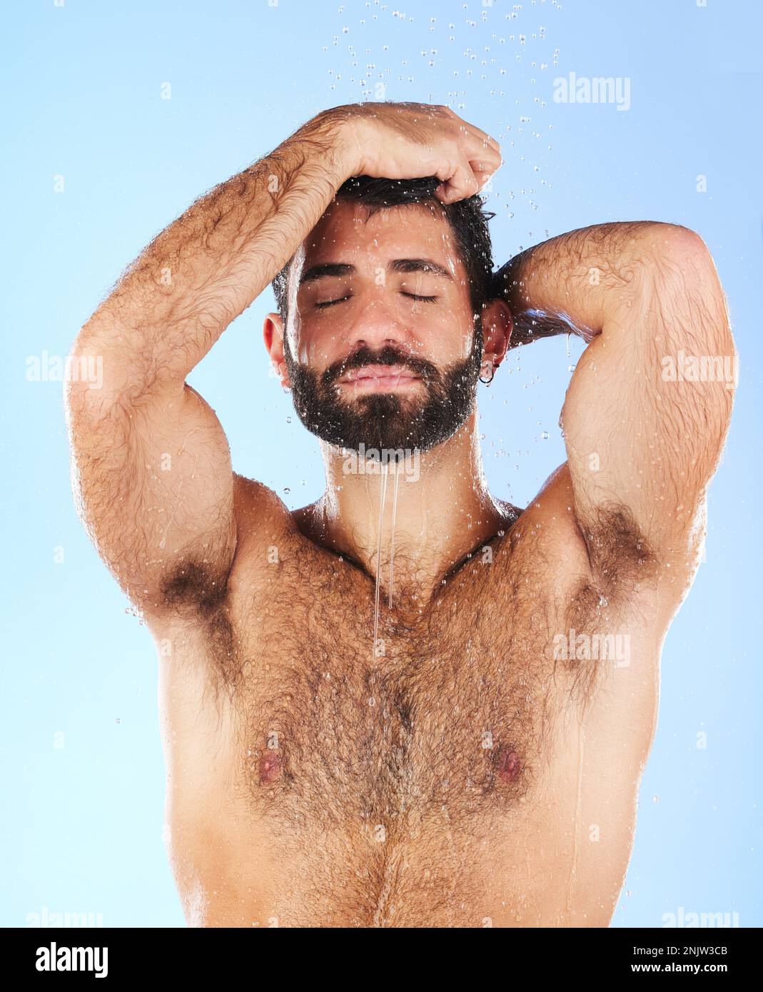 Man, shower and water drop for self care, hygiene and cleaning on a blue background in studio ...