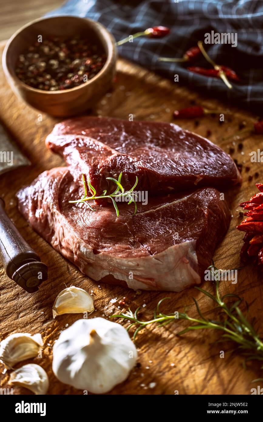 Two beef steaks on a butcher board surrounded by spices, herbs and ...