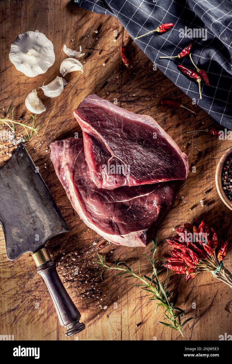 Two beef steaks on a butcher board surrounded by spices, herbs and ...