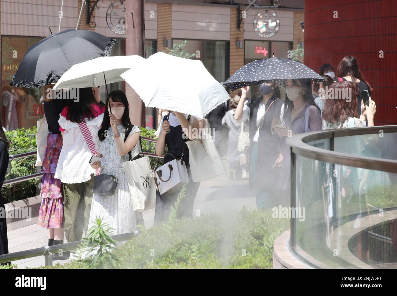 Pedestrians opening a parasol receive a mist spray to cool down on a ...