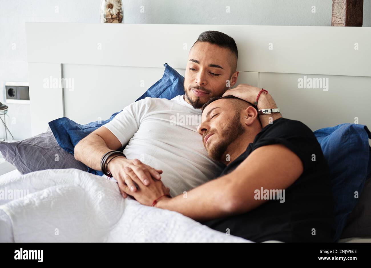 Male couple holding hands and cuddling while lying in bed together at ...