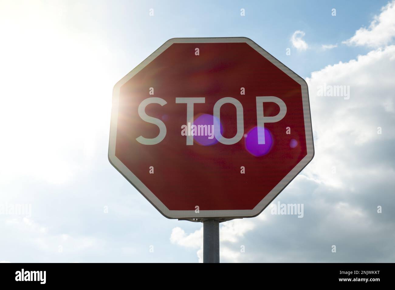 Red stop sign on metal pole on street. Road attention sign on cloudy ...