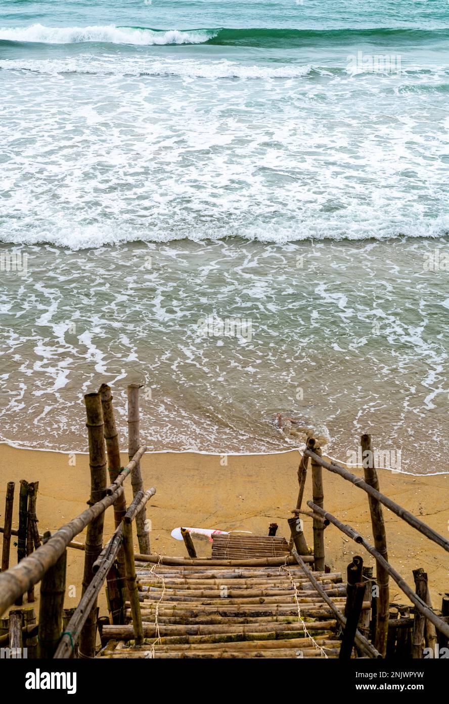 On top of bamboo stairs looking down at the beach and ocean water for ...
