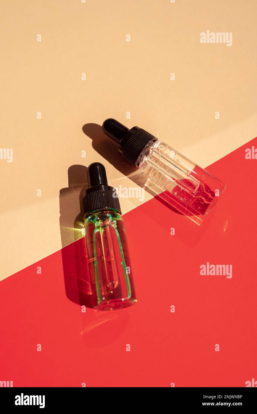 Two glass bottles with cosmetic liquid on bright red background with ...