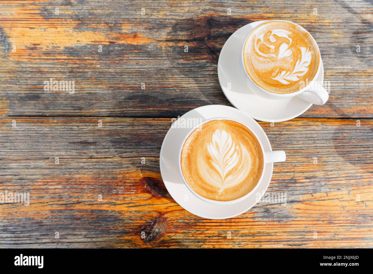 Two latte art cups on white saucers, placed on a rustic wooden table ...