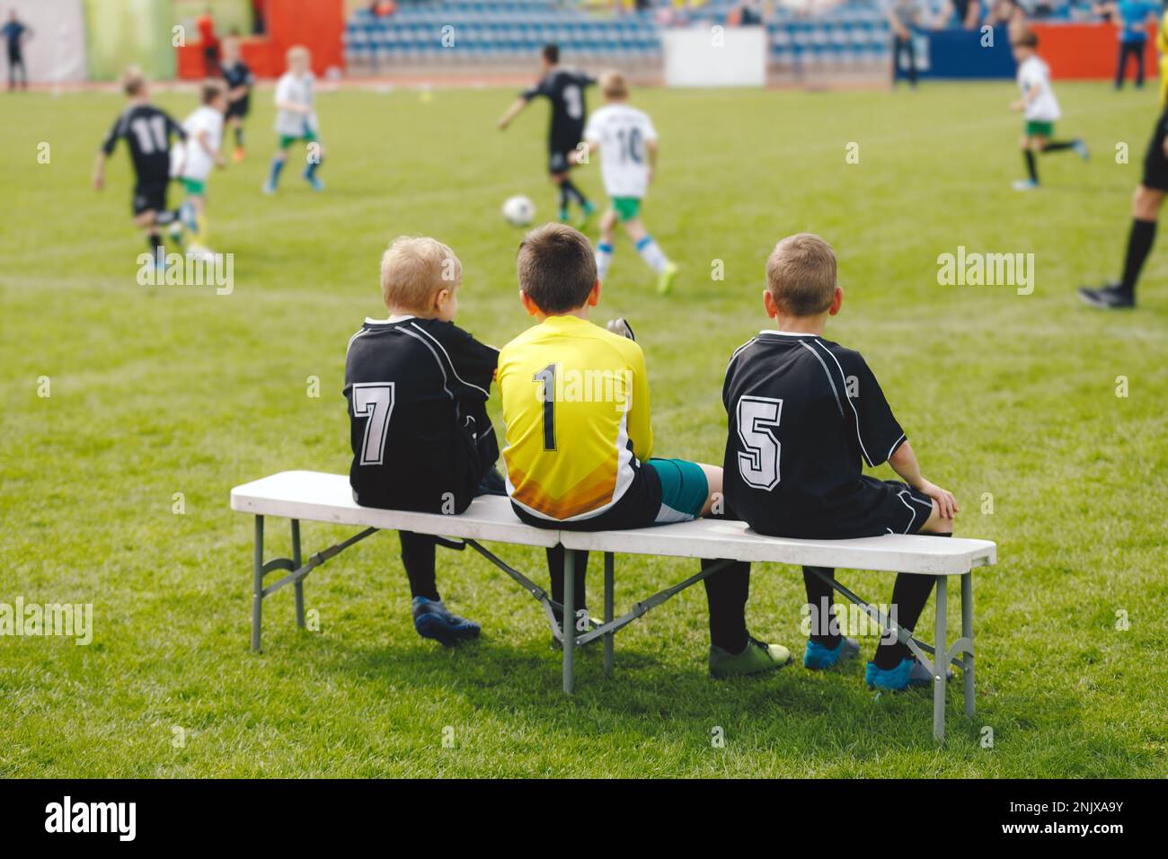 Young boys in soccer jerseys sitting on the substitute players' bench ...