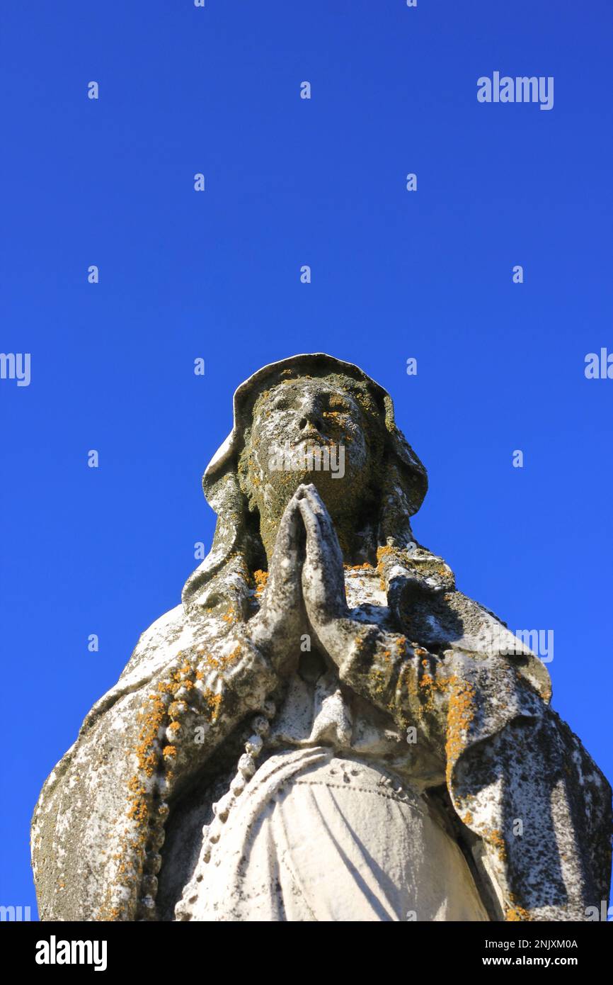 A worn and weathered natural stone statue of the Virgin Mary holding ...
