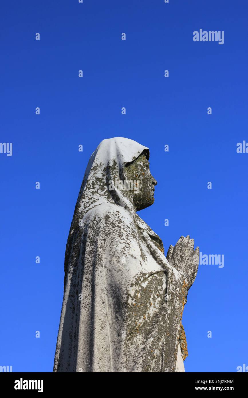 A worn and weathered natural stone statue of the Virgin Mary holding ...