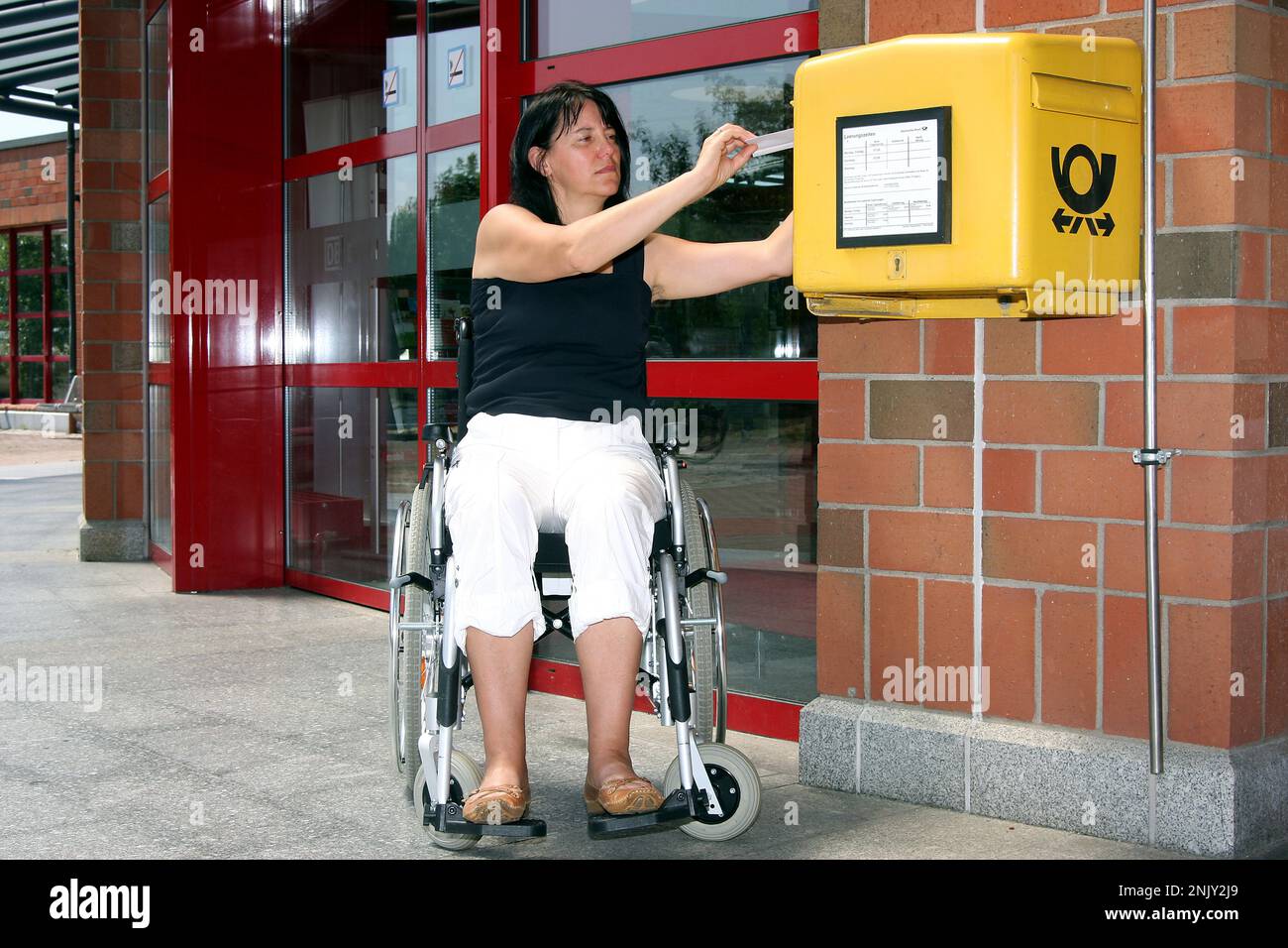 woman in wheelchair throwing mail into a letterbox Stock Photo - Alamy
