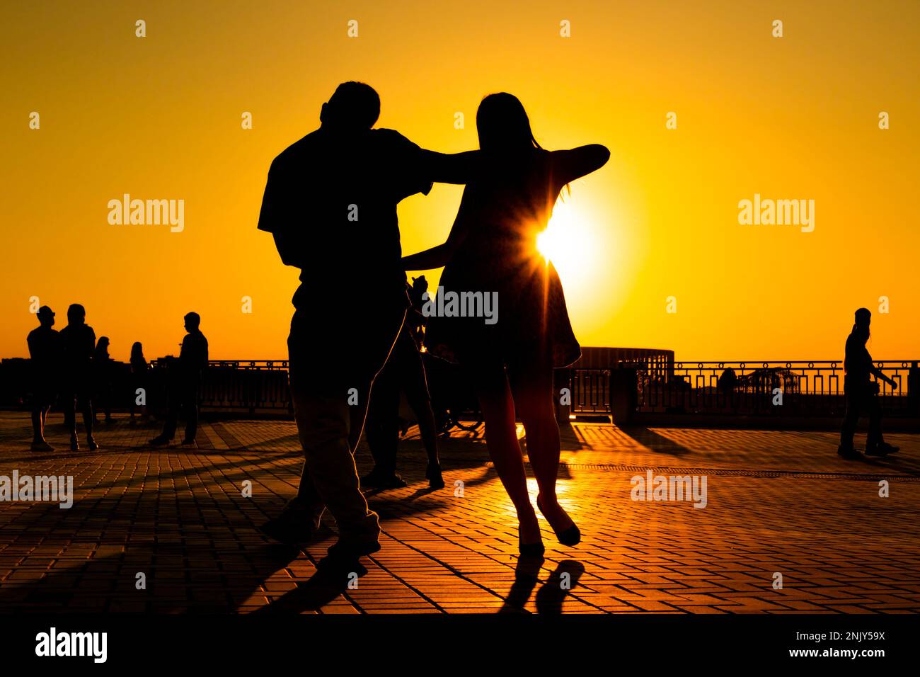 Man and woman couple silhouettes dancing against warm sunset orange sky ...