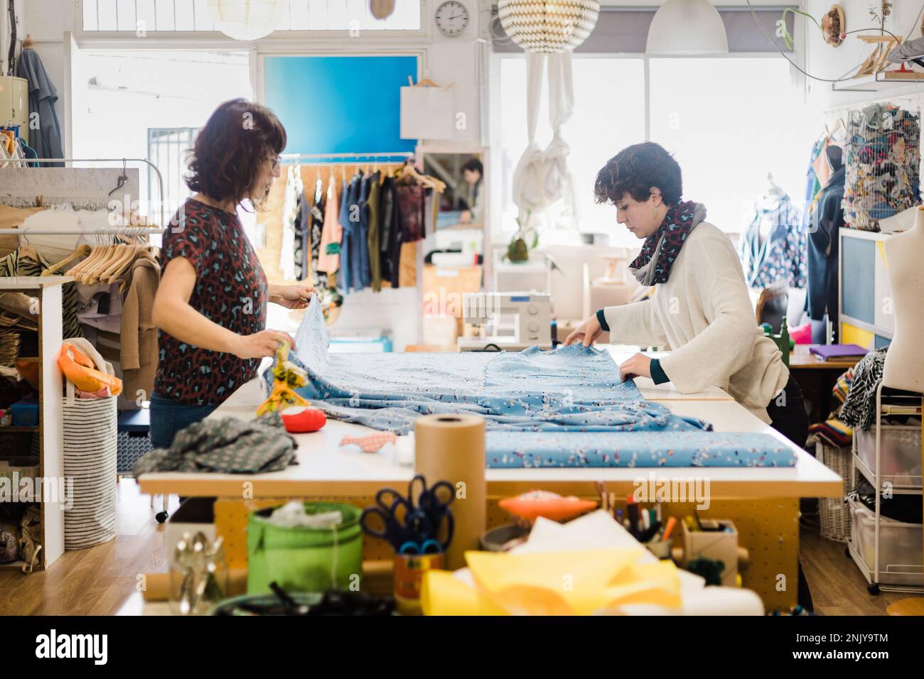 Focused female tailors in casual clothes preparing pattern while working with colorful fabric in ...