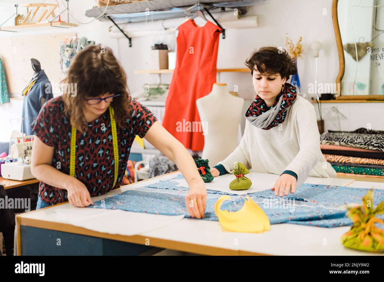 Focused female tailors in casual clothes preparing pattern while working with colorful fabric in ...