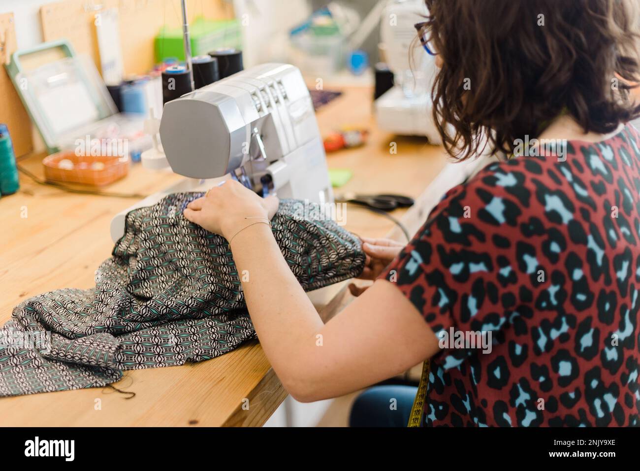 Back view of unrecognizable female tailor putting thread into sewing ...
