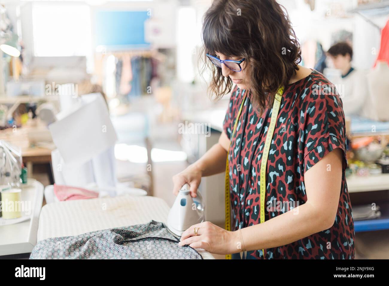 Side view of focused female dressmaker with measuring tape on neck ...