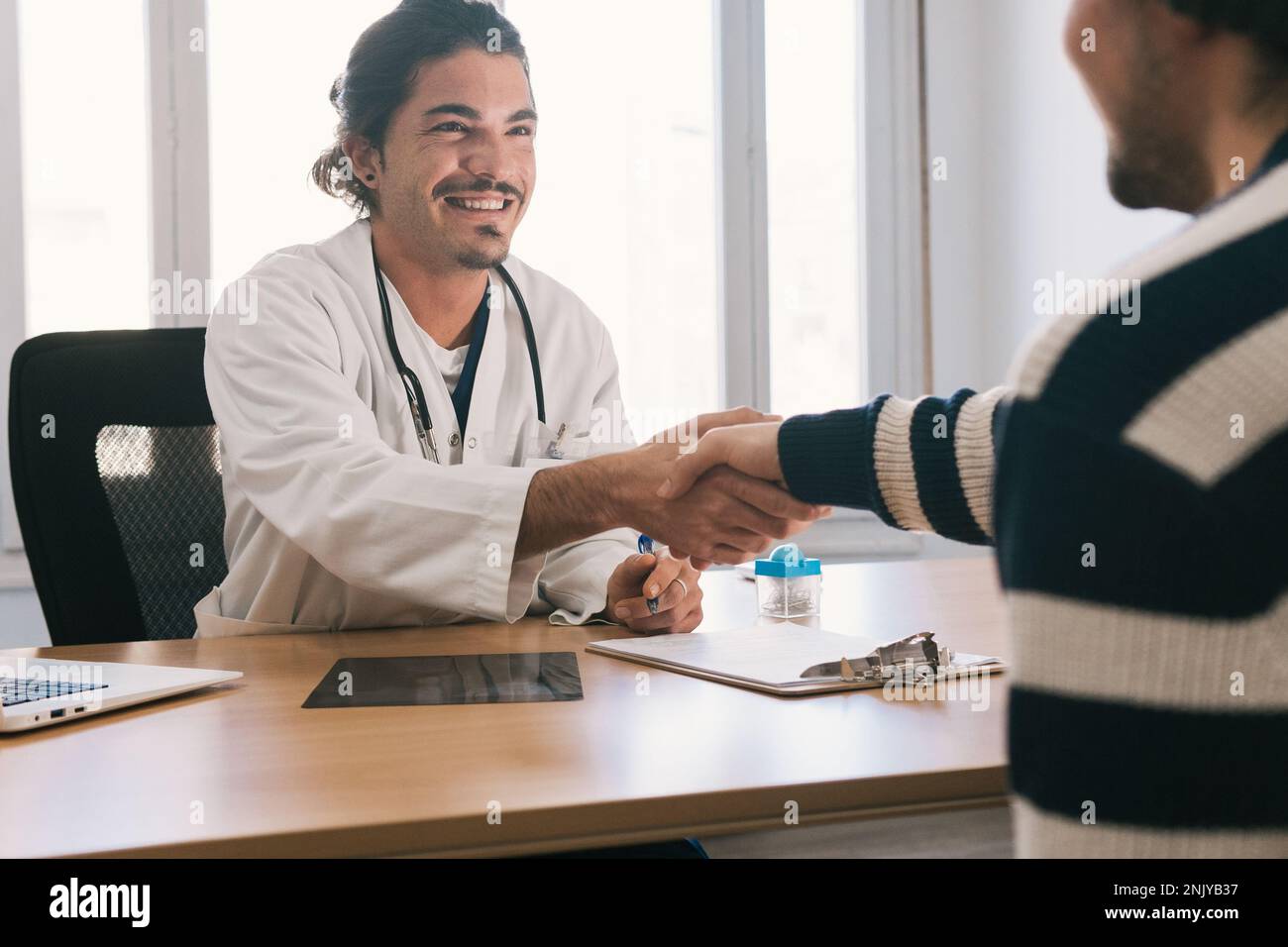 Happy ethnic male doctor in medical uniform smiling and shaking hands ...