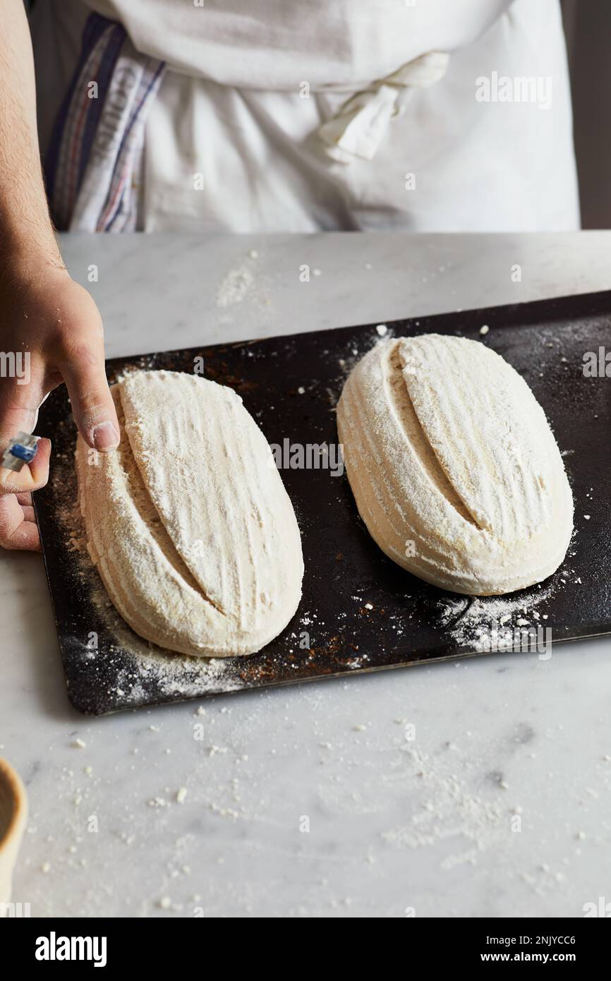 Anonymous baker in apron with blade scoring raw sourdough loaf on table ...