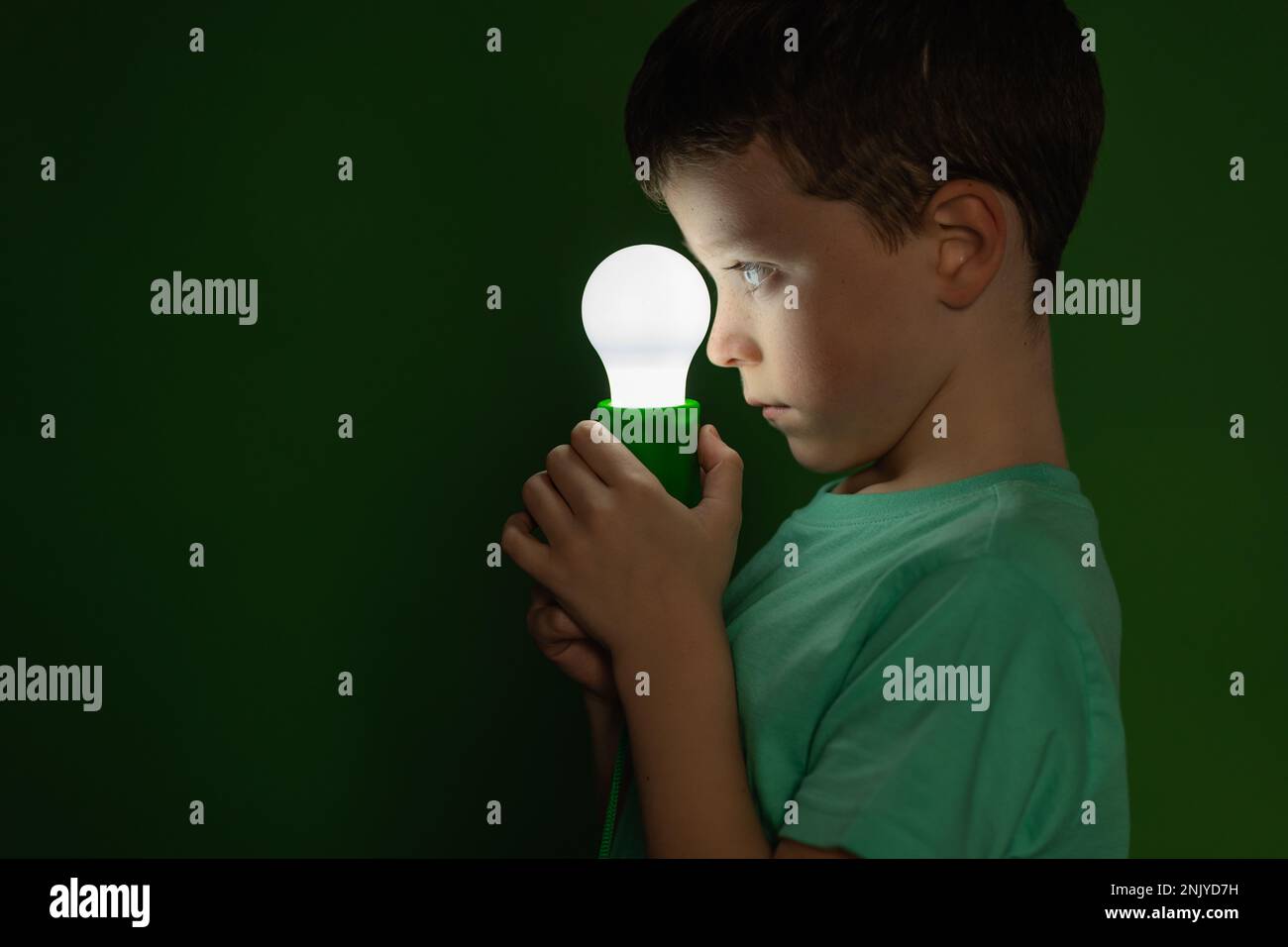 Side view of cute preteen kid in green t shirt standing in dark room ...