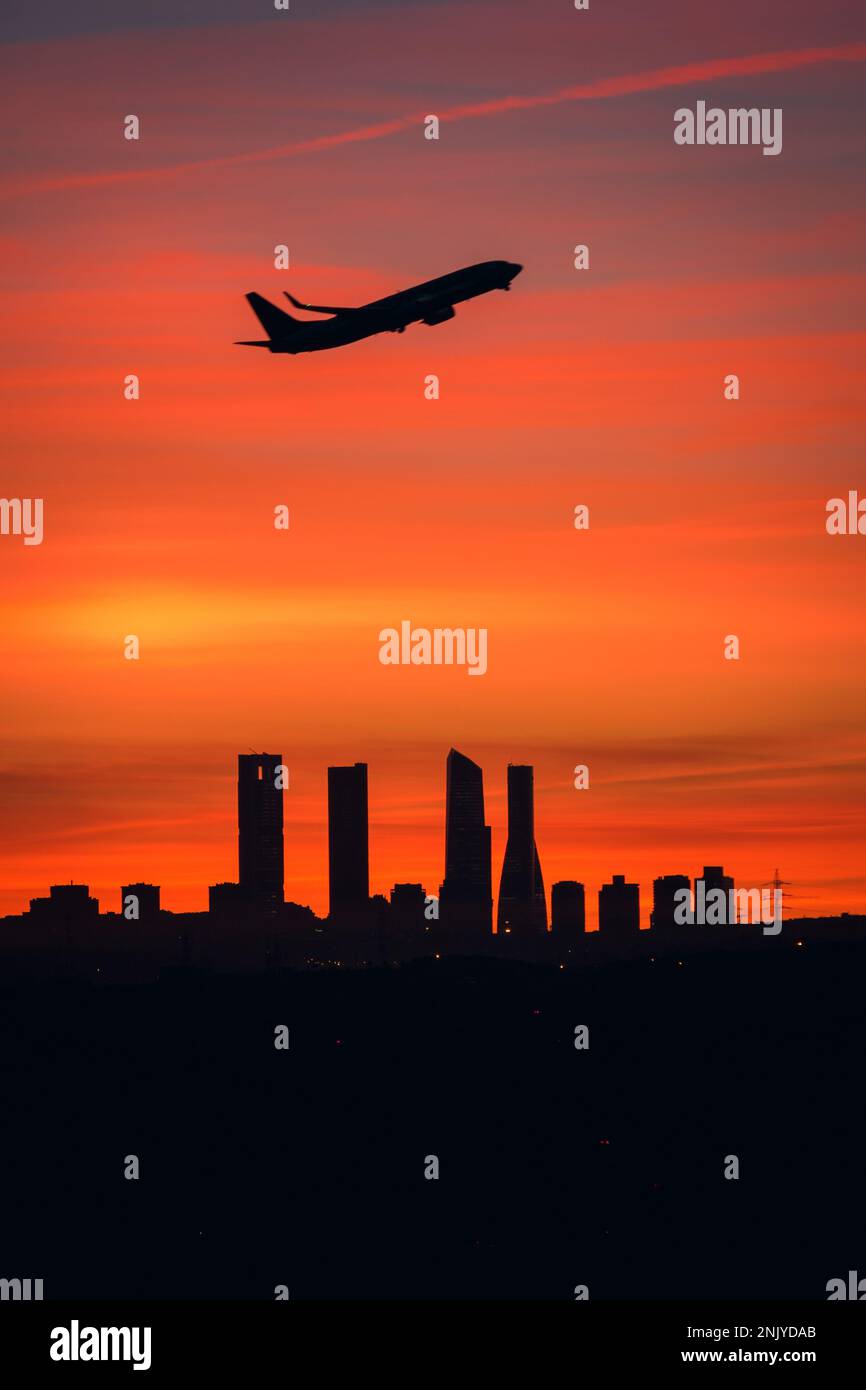 Silhouette of plane flying over cityscape with Four Towers against ...