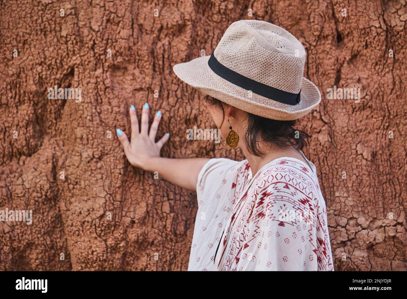Side view of female tourist in hat touching sandy hillside while ...