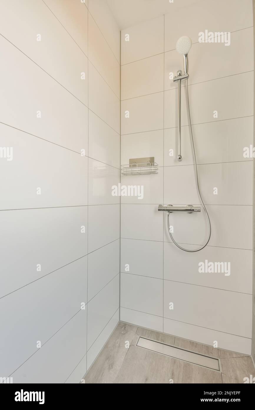 Shower tap hanging on white tiled wall in modern light bathroom at home ...