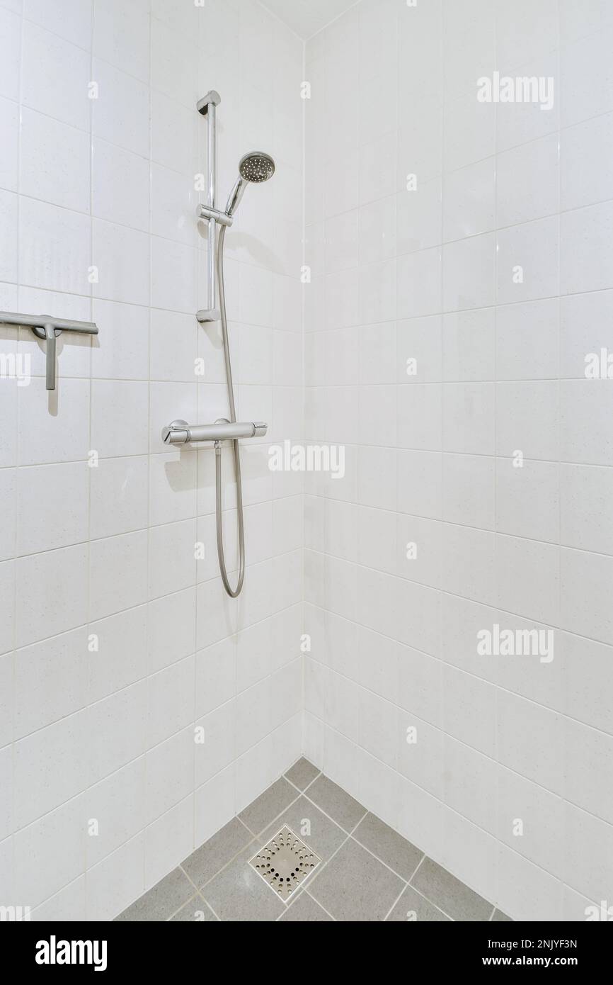 Shower tap hanging on white tiled wall in modern light bathroom at home ...
