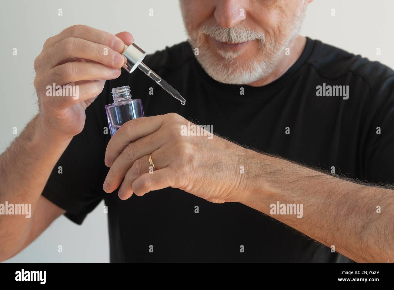 Crop bearded male in black t shirt dropping serum on hand while ...