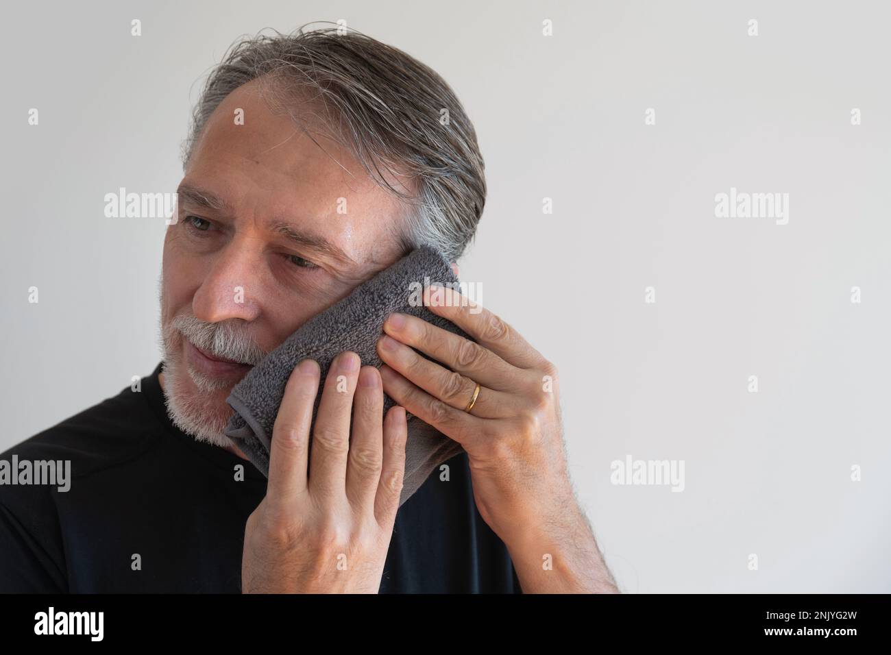 Calm senior male in black t shirt rubbing face with towel while ...