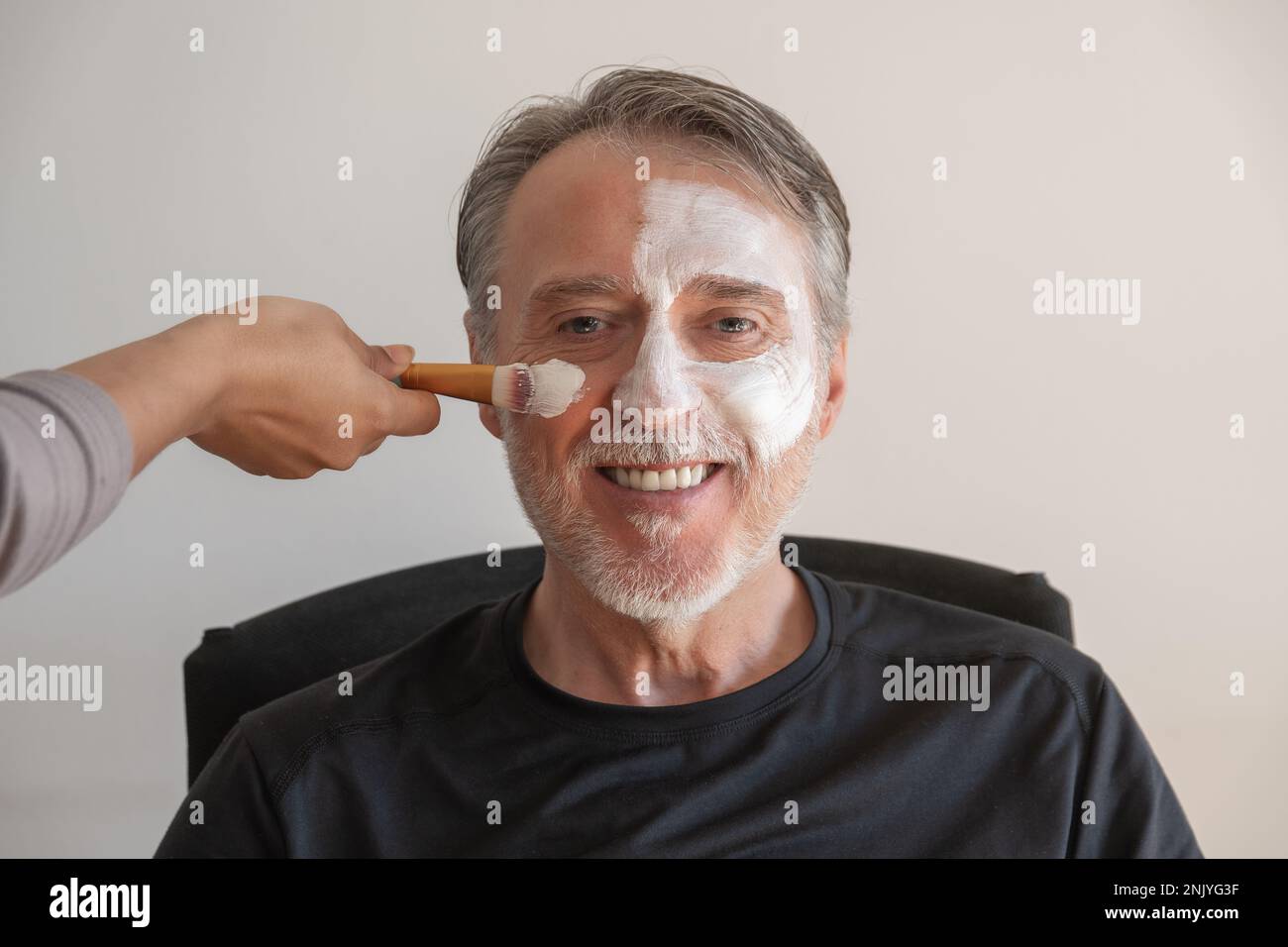 Faceless female applying facial mask with brush on face of cheerful ...