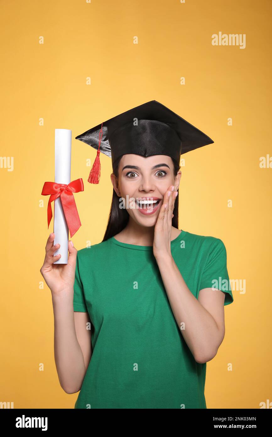 Emotional student with graduation hat and diploma on yellow background ...
