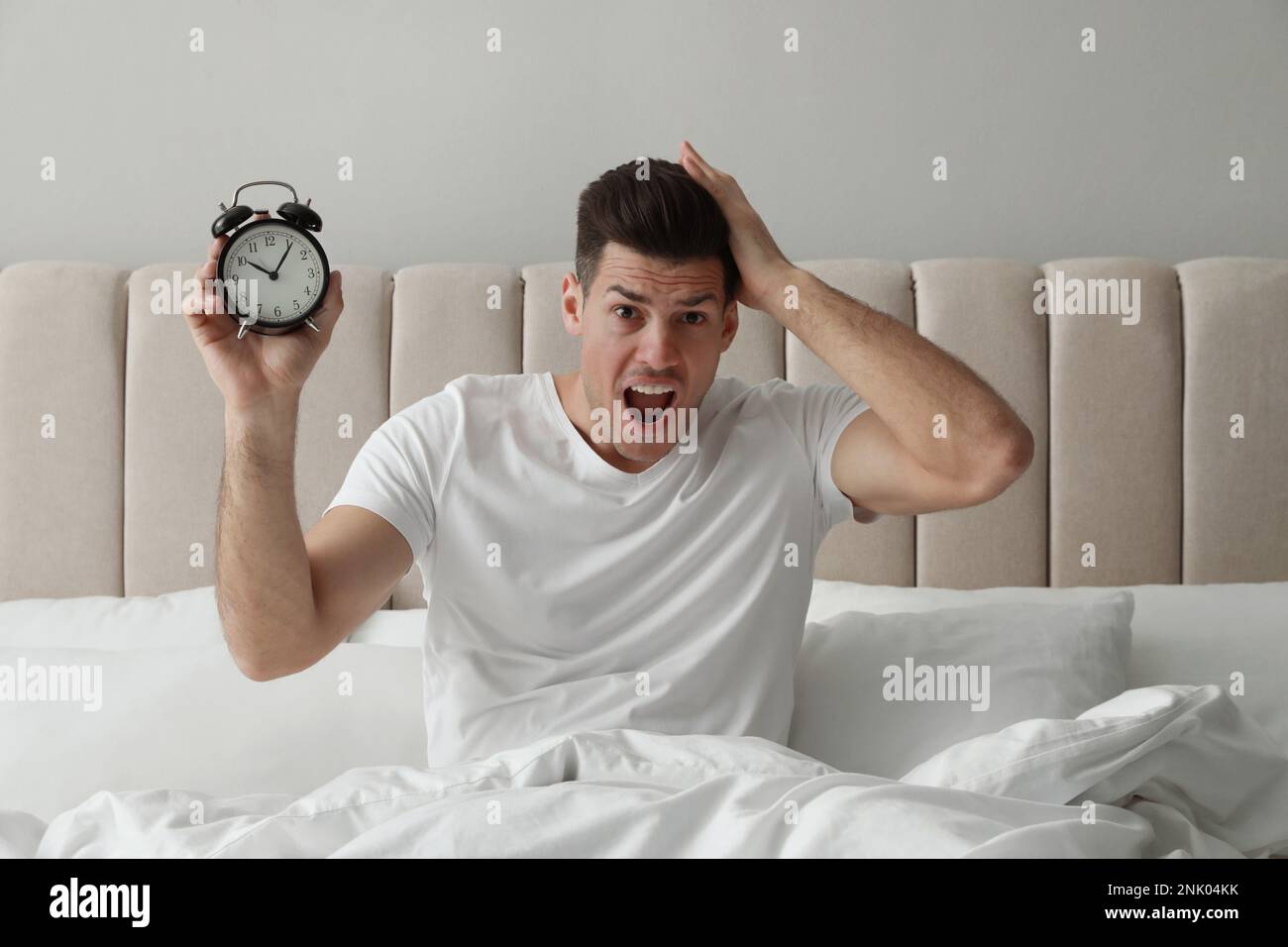 Emotional man with alarm clock in bed. Being late because of ...