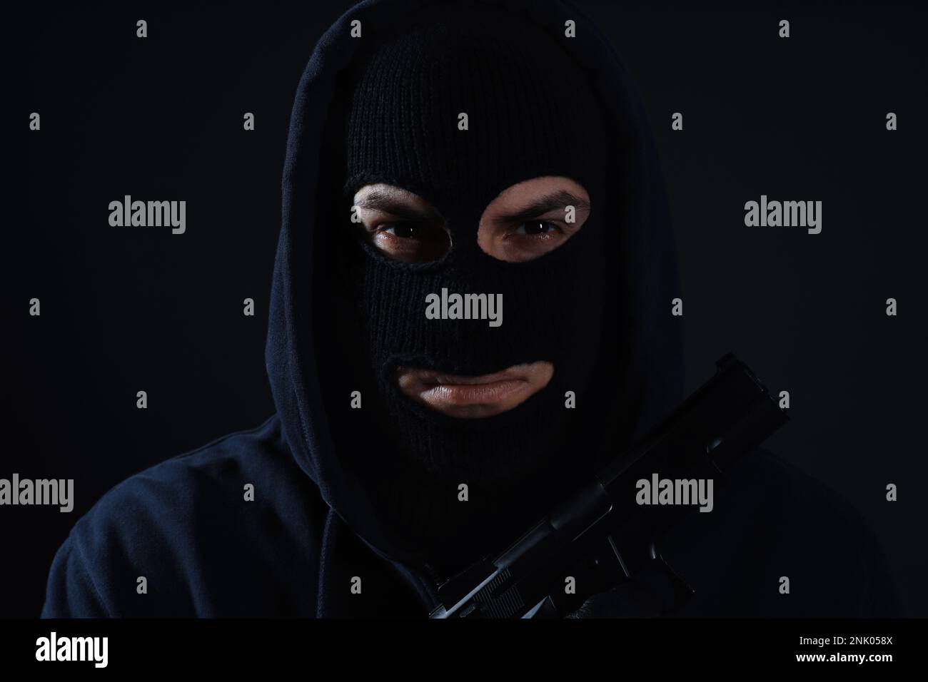 Man wearing knitted balaclava with gun on black background Stock Photo ...