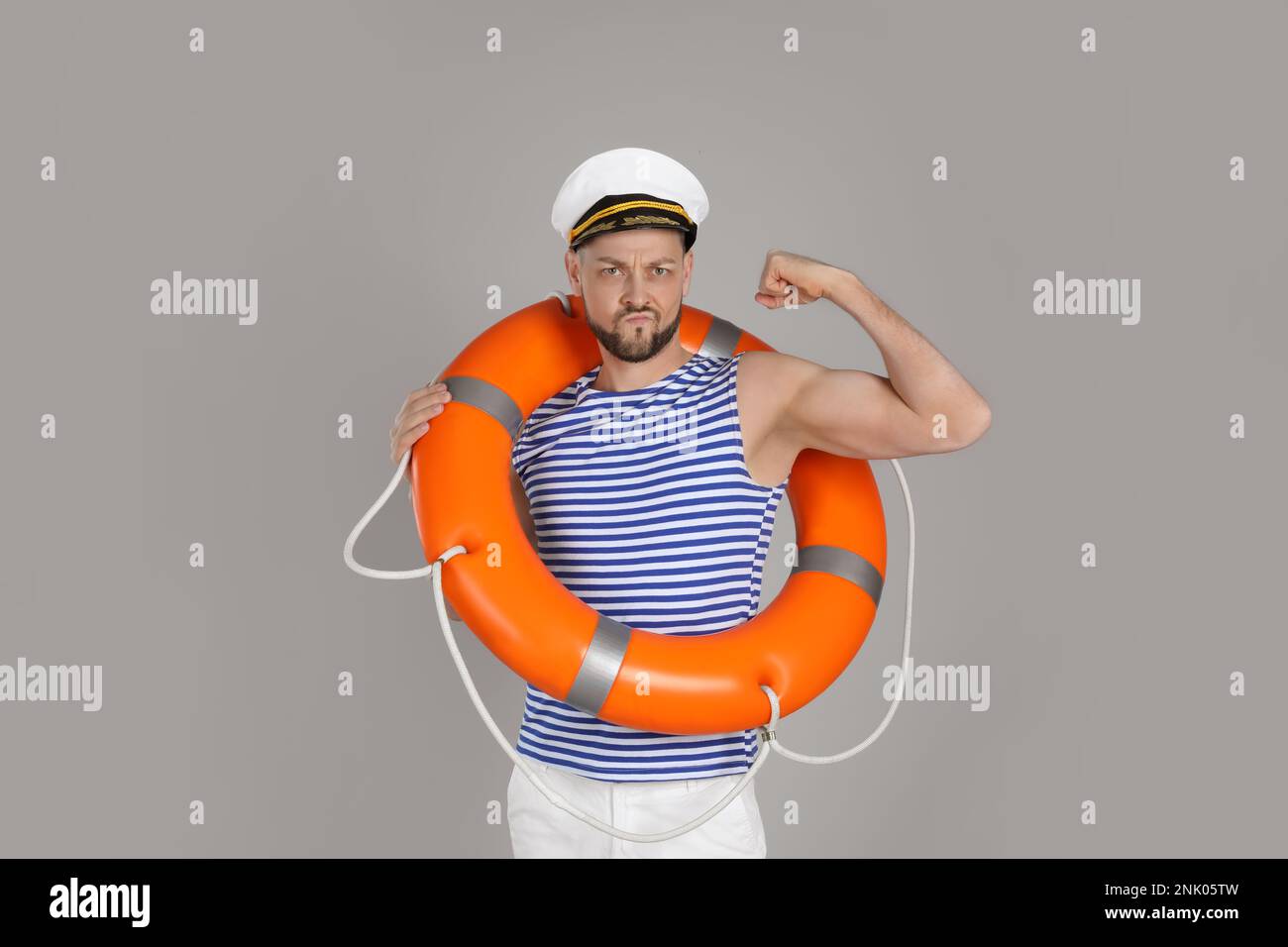 Strong sailor with orange ring buoy showing biceps on grey background ...