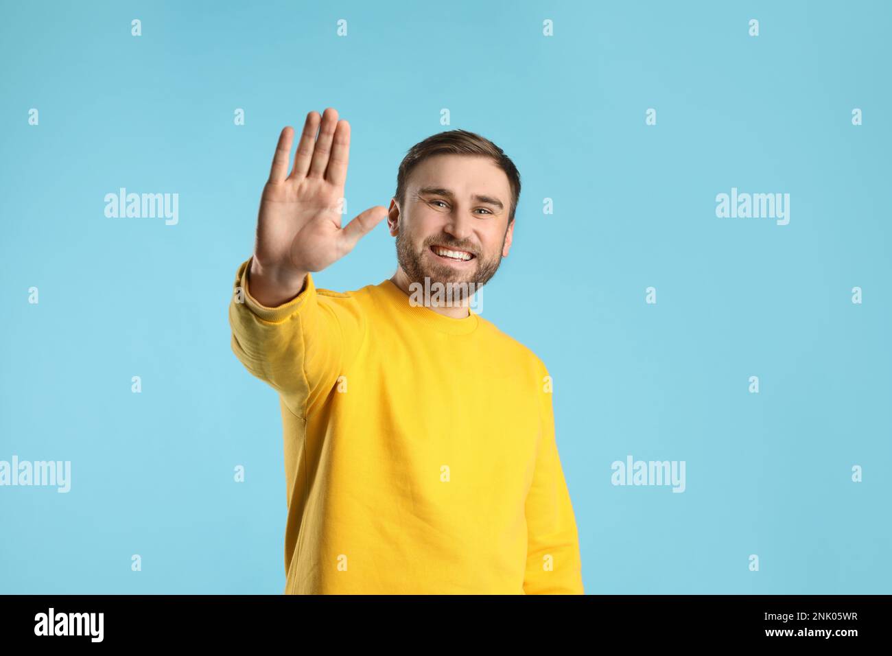 Happy young man waving to say hello on light blue background Stock ...