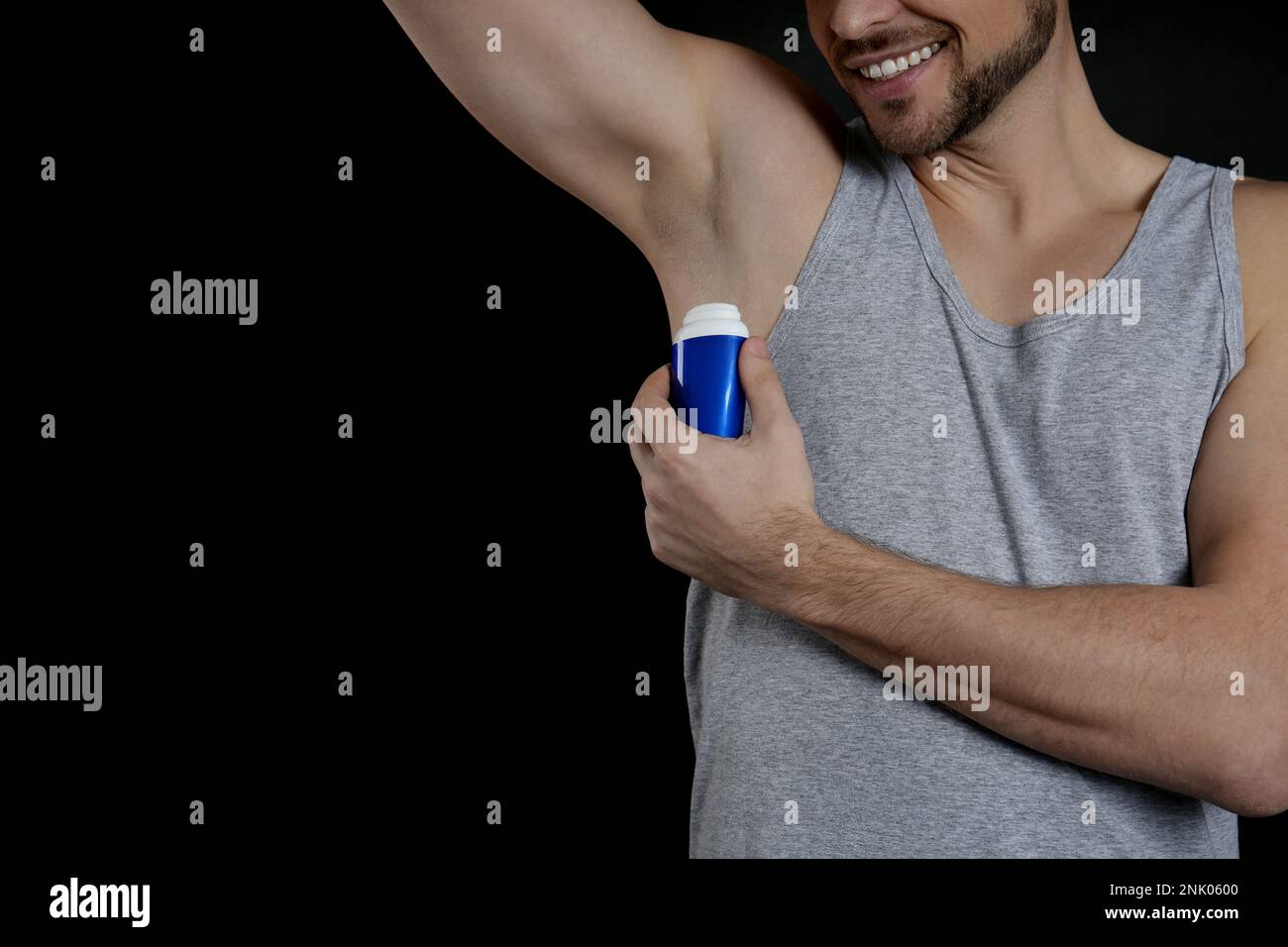 Man applying deodorant on black background, closeup. Space for text ...